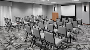 Uma sala de conferências com fileiras de cadeiras, um pódio e uma tela de projeção.