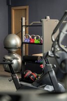 Uma academia com equipamentos de ginástica, incluindo halteres, um banco de musculação e uma bicicleta ergométrica.