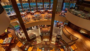 Restaurante em vários níveis, com pisos de madeira e guarda-corpos de vidro, apresentando diversas áreas de refeição e um espaço central para sentar.