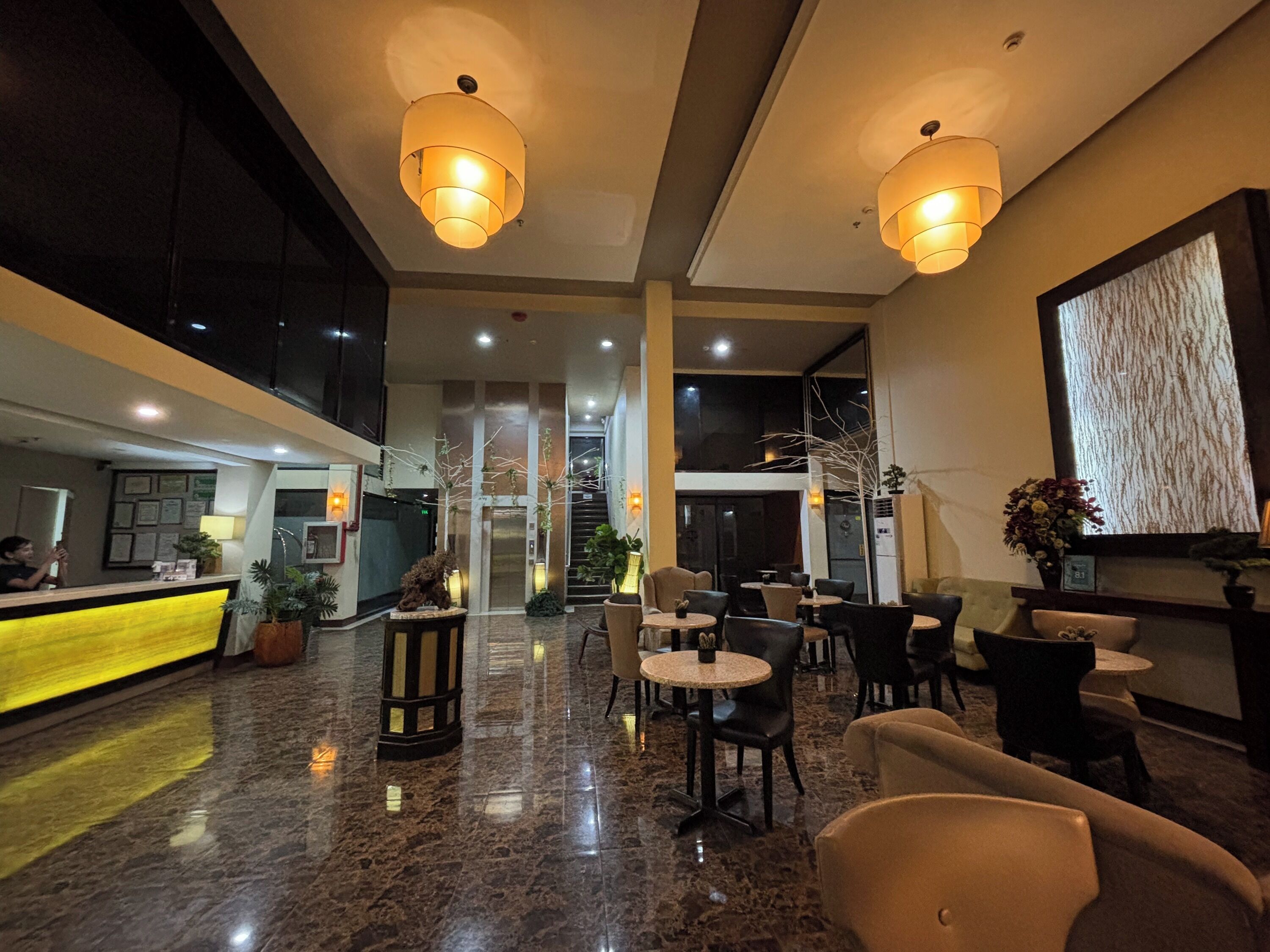 Um saguão de hotel com balcão de recepção, área de estar e escadas para um andar superior.