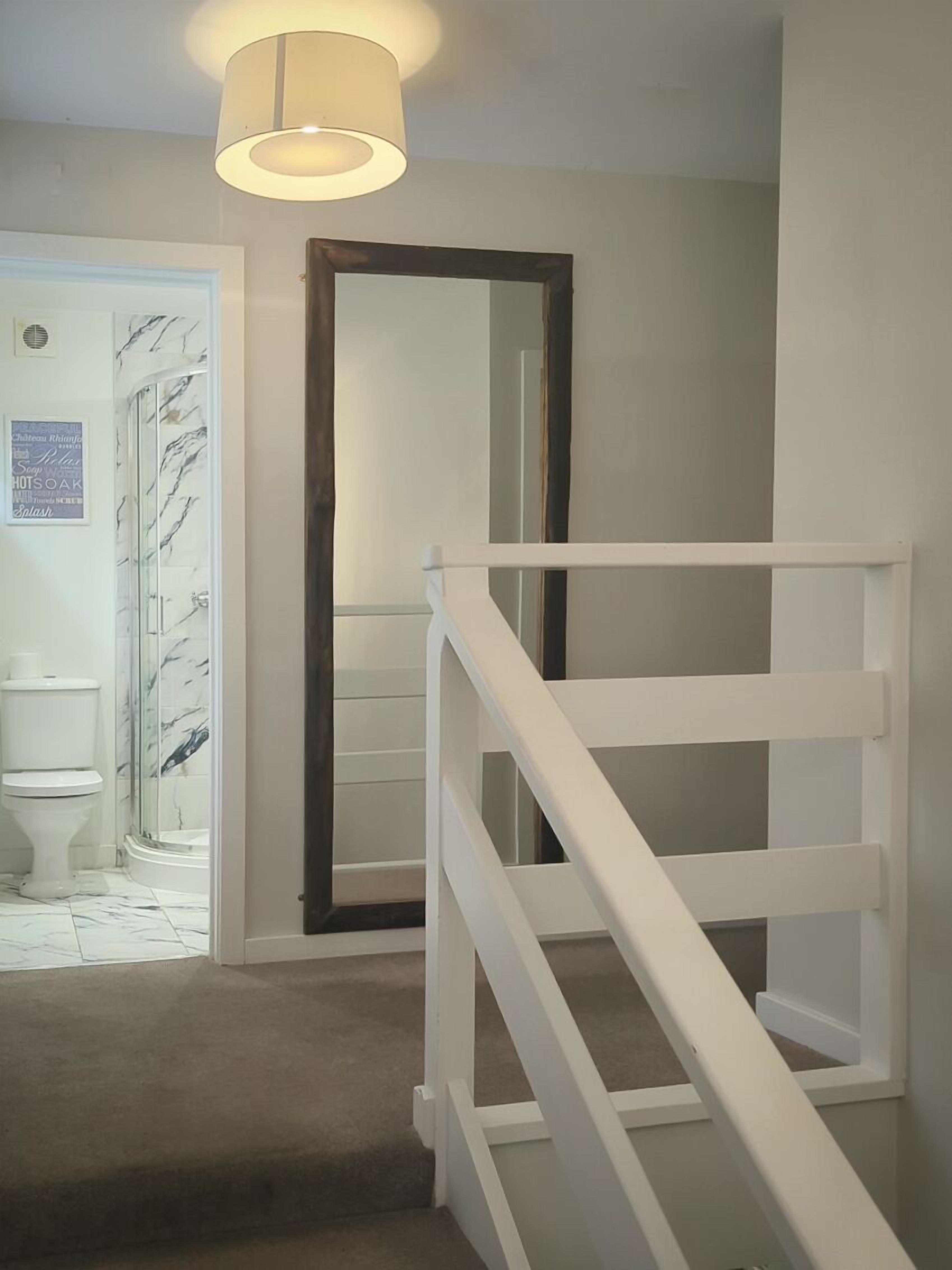 Uma escadaria com corrimãos brancos que leva a um banheiro com chuveiro e vaso sanitário.