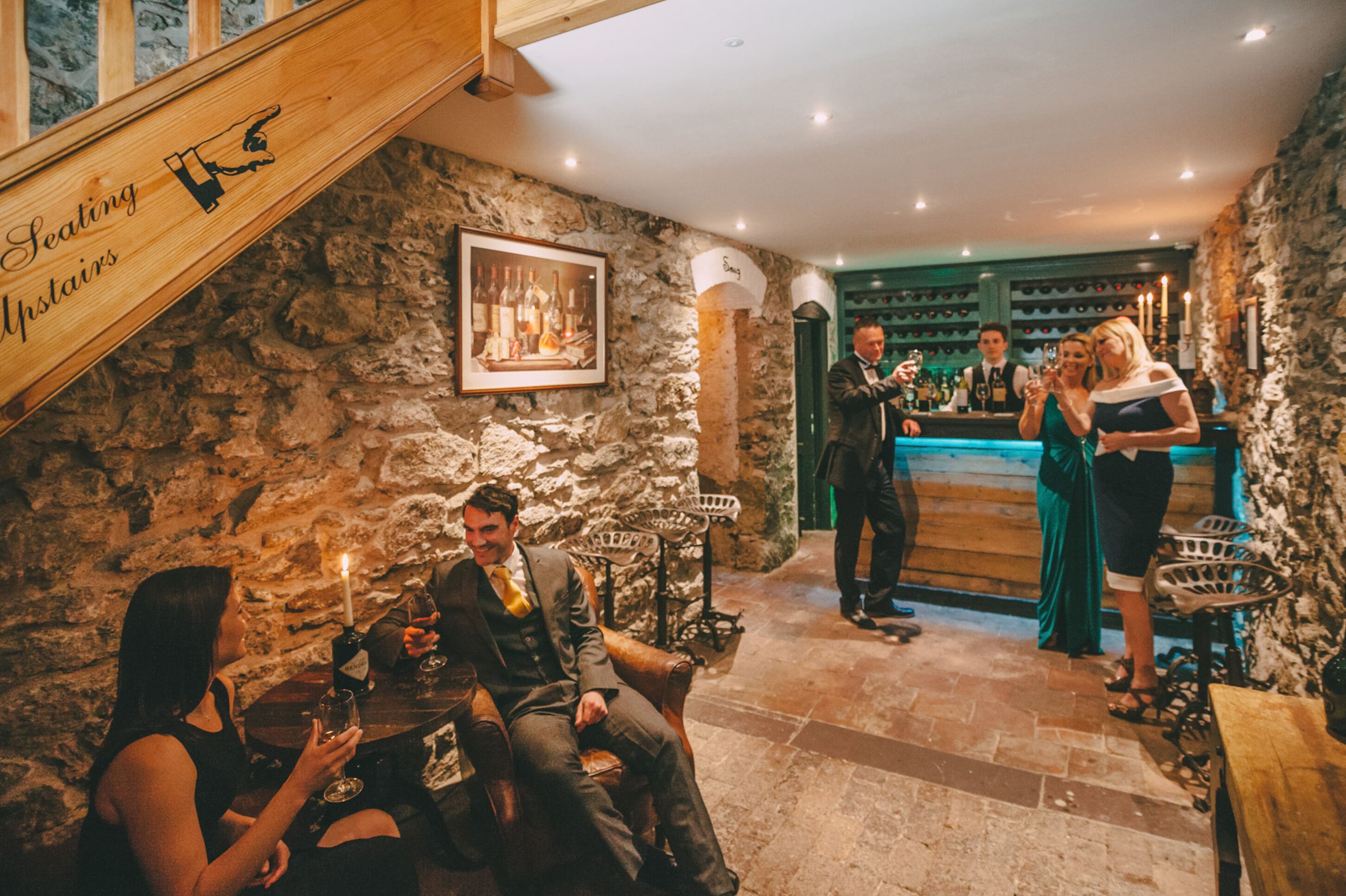Um quarto com paredes de pedra, área de bar, assentos e escada com a inscrição 'Seating Upstairs'.