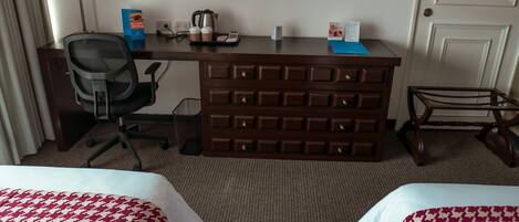 Quarto de hotel com duas camas, uma escrivaninha com cadeira, televisão, minibar e uma porta.