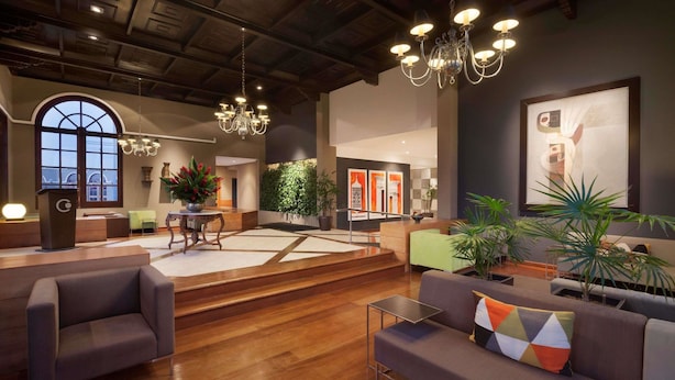 Um hall moderno com piso de madeira, balcão de recepção, escada e áreas de estar.