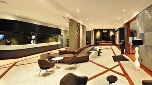 Um lobby moderno com balcão de recepção, área de estar e escadaria para um andar superior.