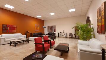 Um hall amplo com um sofá branco, poltronas vermelhas, uma mesa de centro e um vaso de planta.