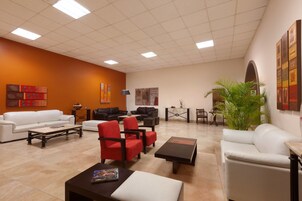 Um hall amplo com um sofá branco, poltronas vermelhas, uma mesa de centro e um vaso de planta.