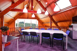 Uma sala de conferências com uma longa mesa, cadeiras azuis e teto de madeira.