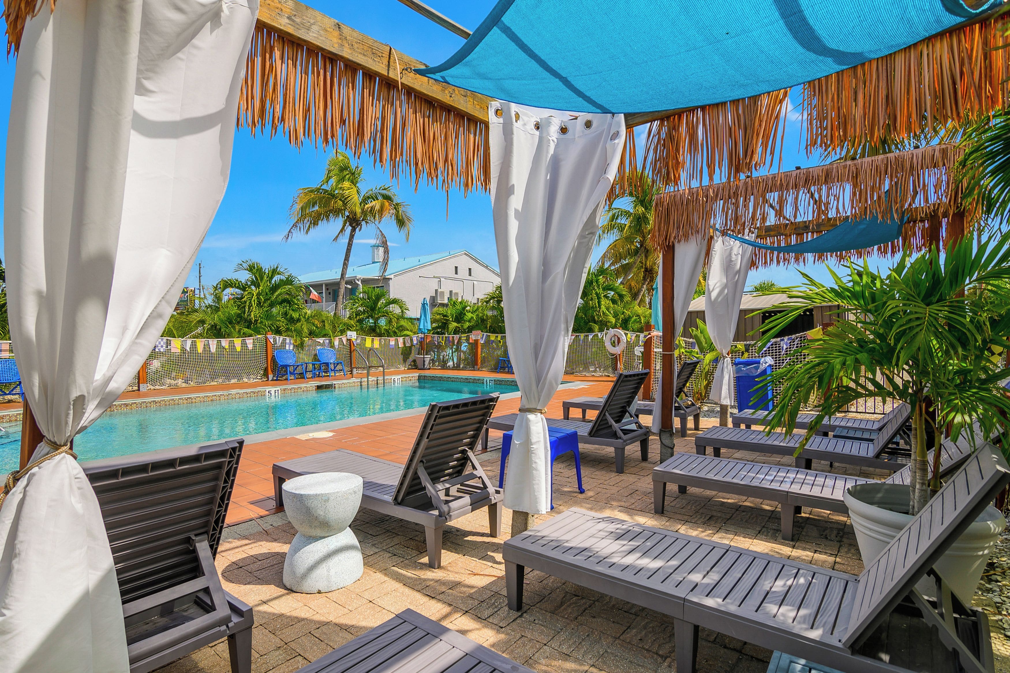 Uma área ao lado da piscina com espreguiçadeiras, uma mesa pequena e vista clara da piscina.