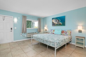 Quarto com cama, janela com cortinas, ar condicionado fixado na parede e pintura de uma tartaruga marinha.