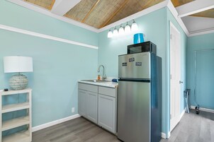 Uma cozinha com paredes azul-claras, uma geladeira de aço inoxidável, uma pia e uma prateleira branca com uma luminária.