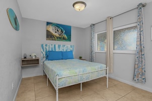 Quarto com cama, um quadro, janela com cortinas e estante com planta.