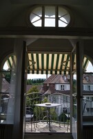 Varanda com mesa e cadeiras, um toldo listrado e vista para casas ao fundo.