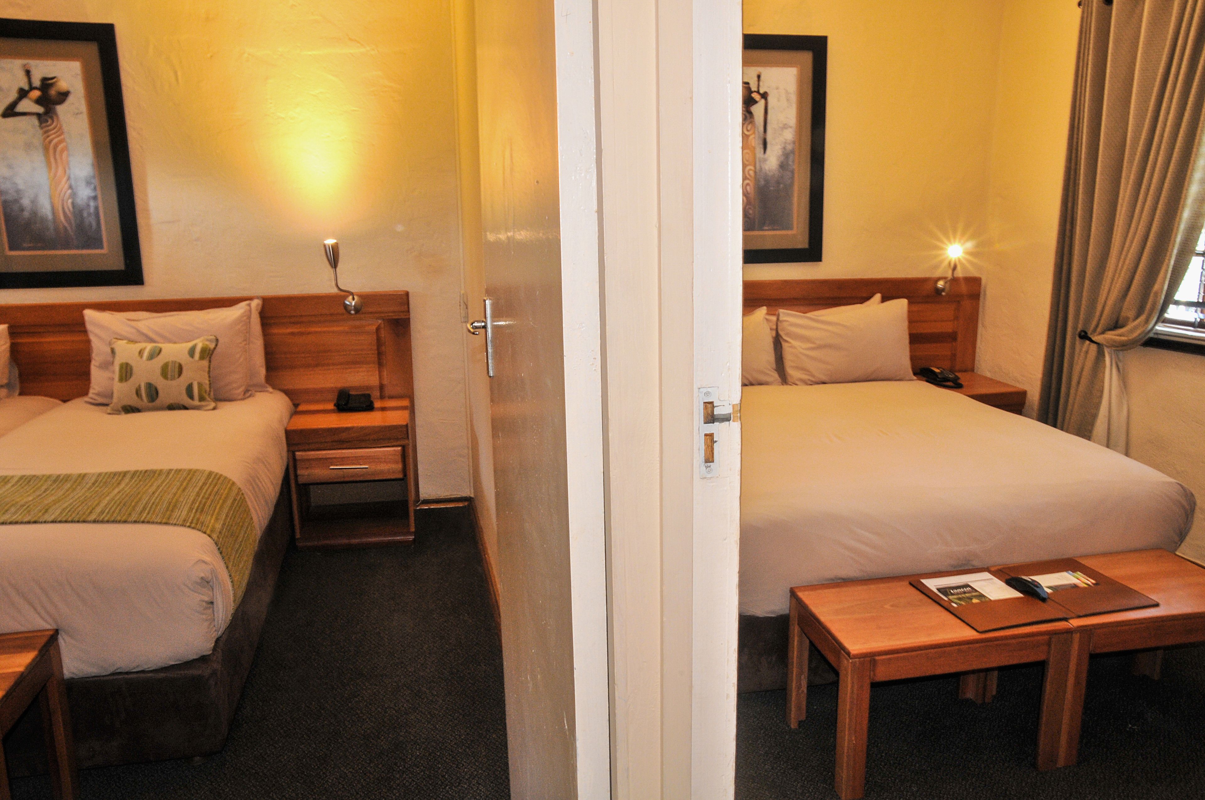Quarto de hotel com duas camas, mesa de cabeceira com abajur, uma pequena mesa e janela com cortinas.