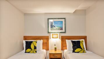 Quarto de hotel com duas camas, uma mesa de cabeceira com abajur e um quadro pendurado na parede.