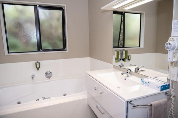 Casa de banho moderna com banheira, lavatório duplo com espelho e secador de cabelo na parede.