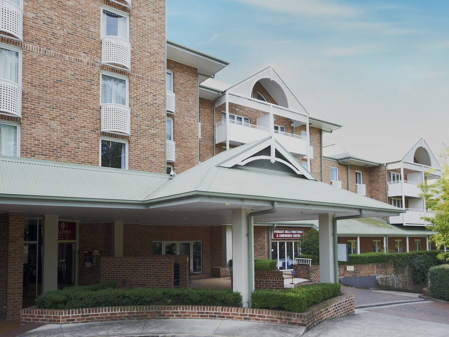 Um hotel com vários andares, fachada de tijolo, varandas brancas e área de entrada coberta.