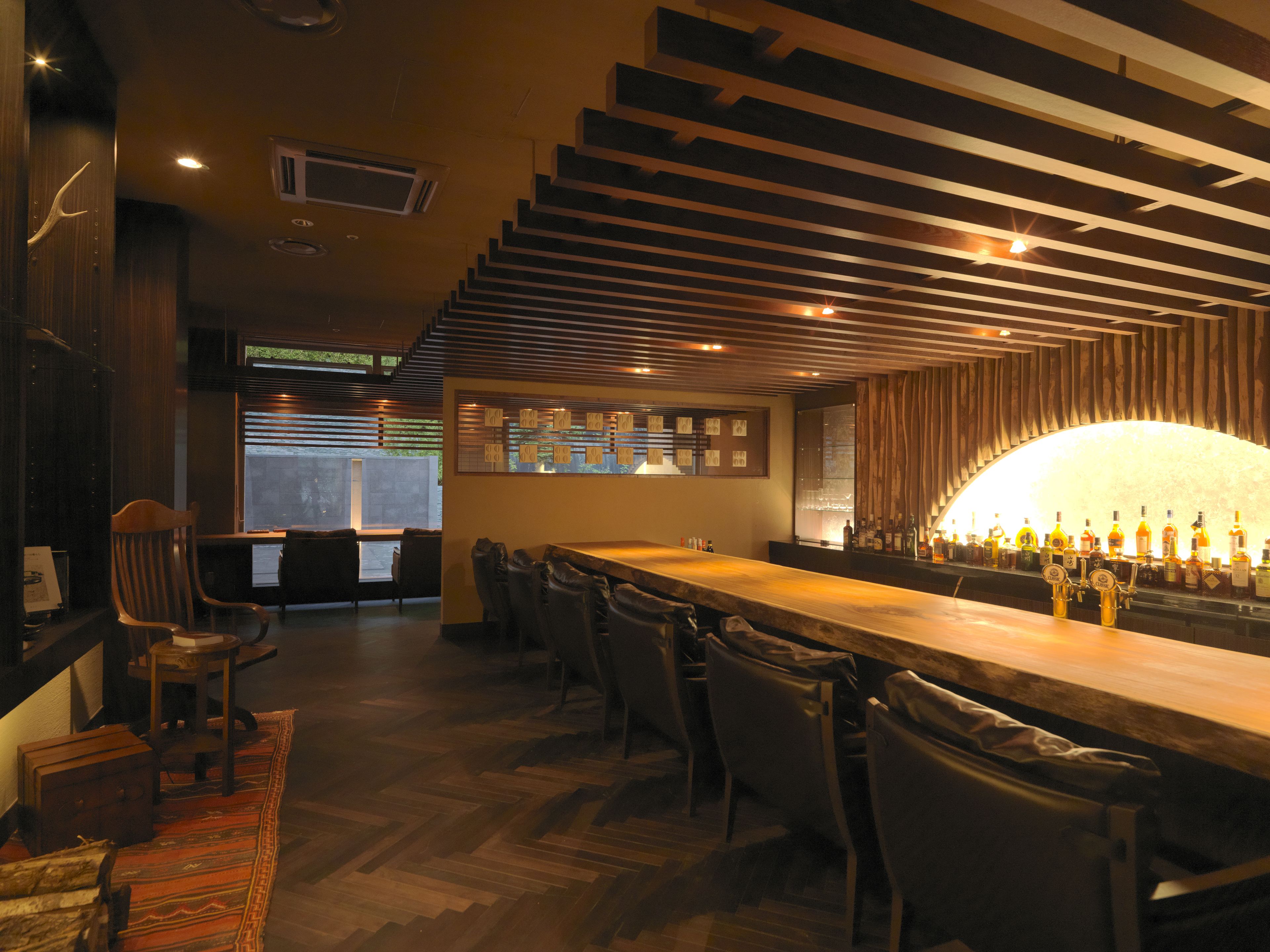 Uma área de bar com um balcão comprido, várias cadeiras e um teto de madeira com design em ripas.