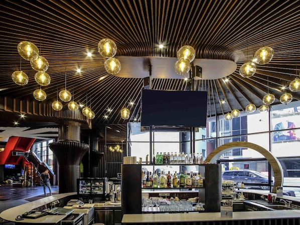 Um bar moderno com balcão curvo, uma tela de TV grande e diversas garrafas de bebidas alcoólicas.