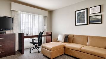 Quarto de hotel moderno com sofá de couro marrom, escrivaninha de madeira, televisão e quadros nas paredes.