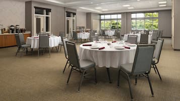 Sala de conferência com mesas redondas, cadeiras e uma área de buffet.