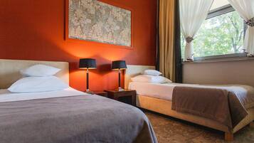 Quarto de hotel com duas camas, um quadro grande na parede e uma janela com cortinas.