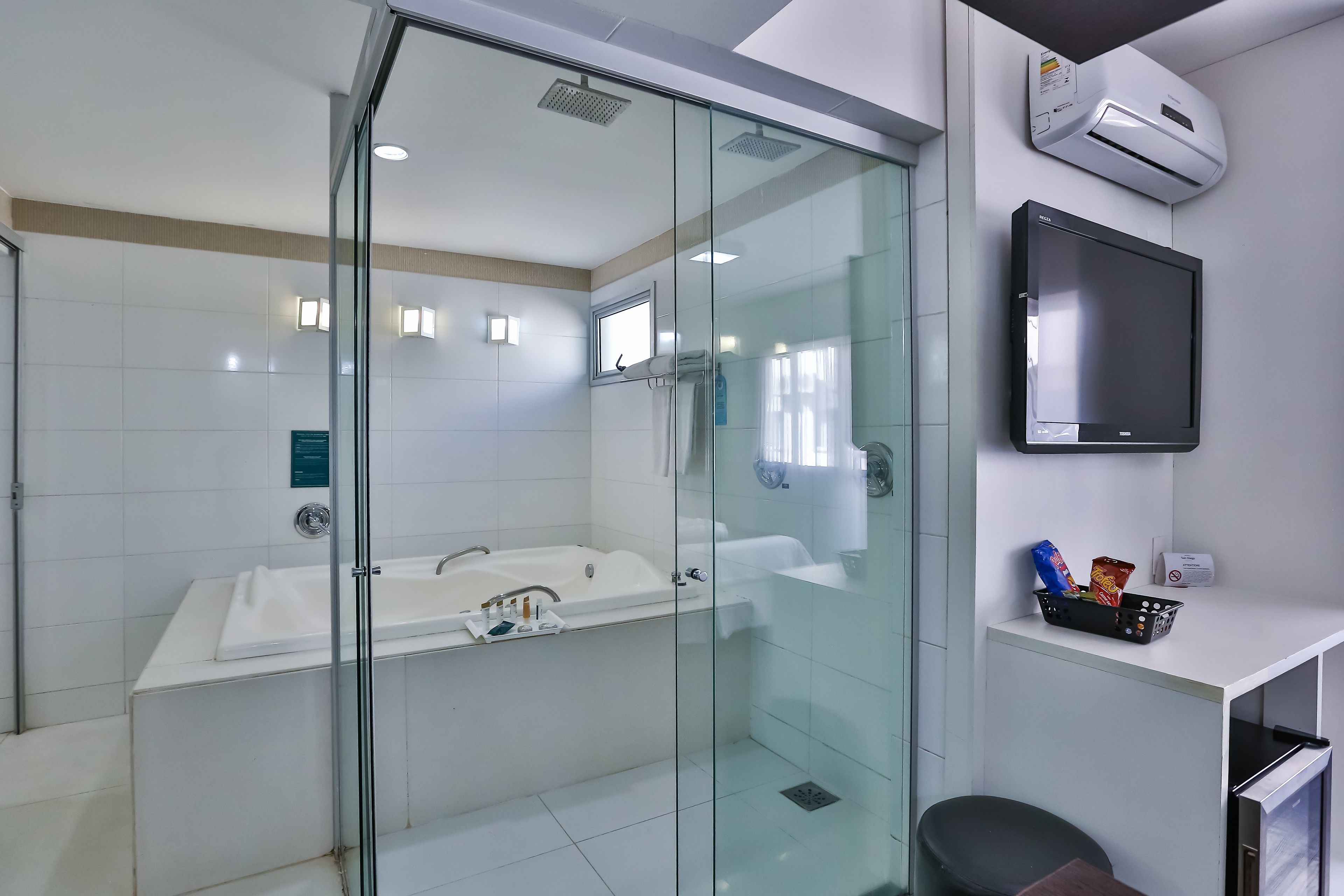 Uma casa de banho moderna com chuveiro envolto em vidro, uma banheira grande e uma televisão fixada na parede.