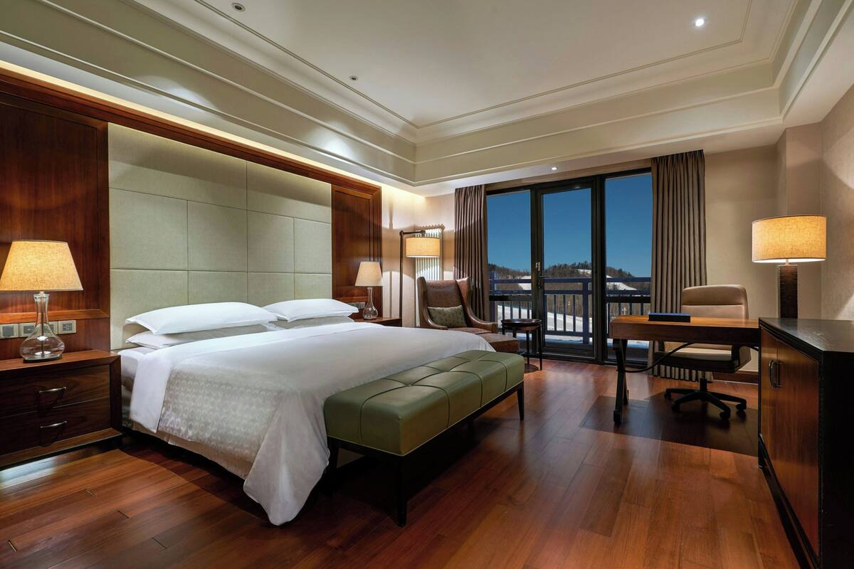 Quarto de hotel com uma cama grande, uma escrivaninha e vista para a cidade.