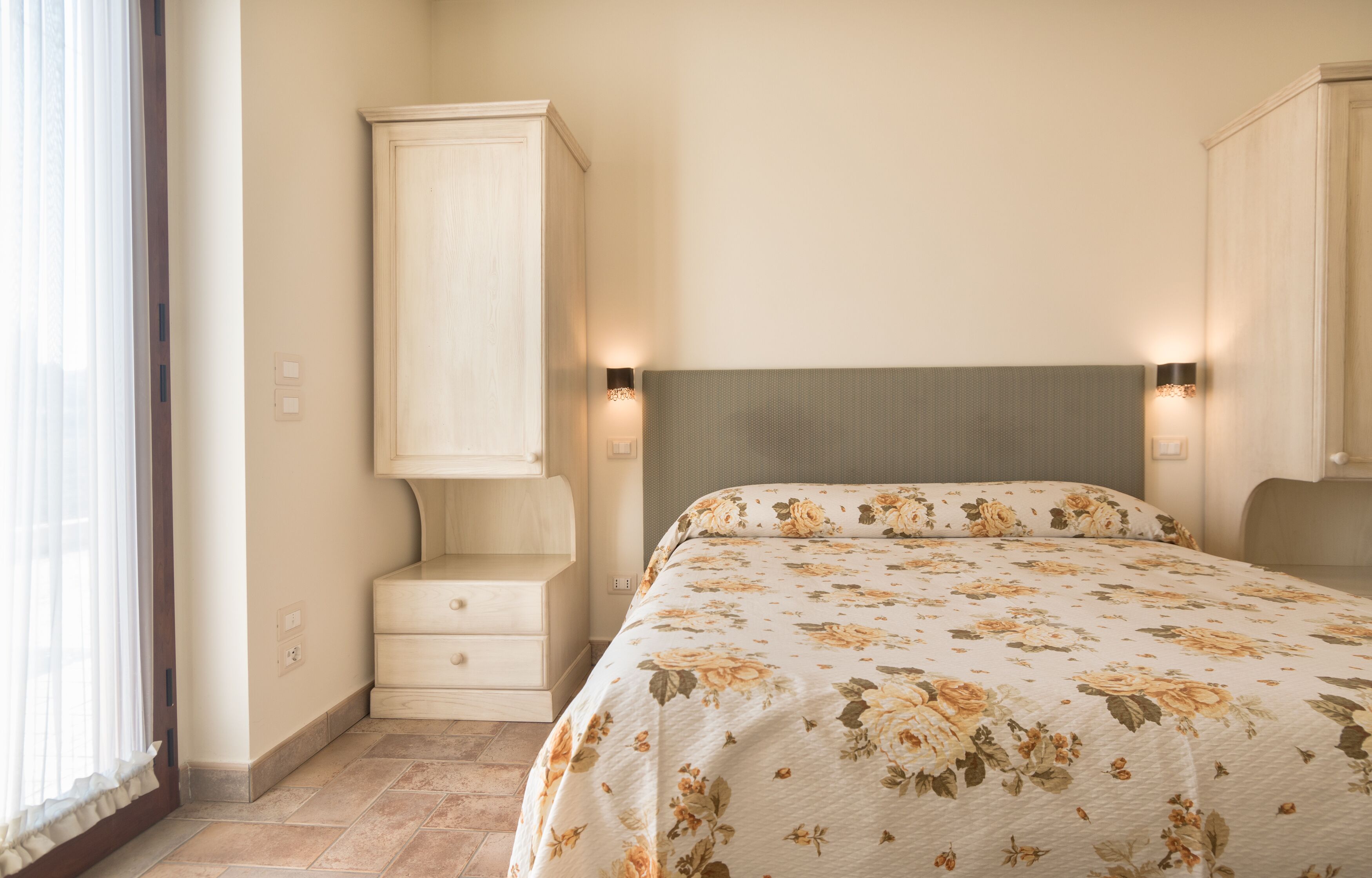 Quarto com cama, mesa de cabeceira, cômoda e duas luminárias na parede.