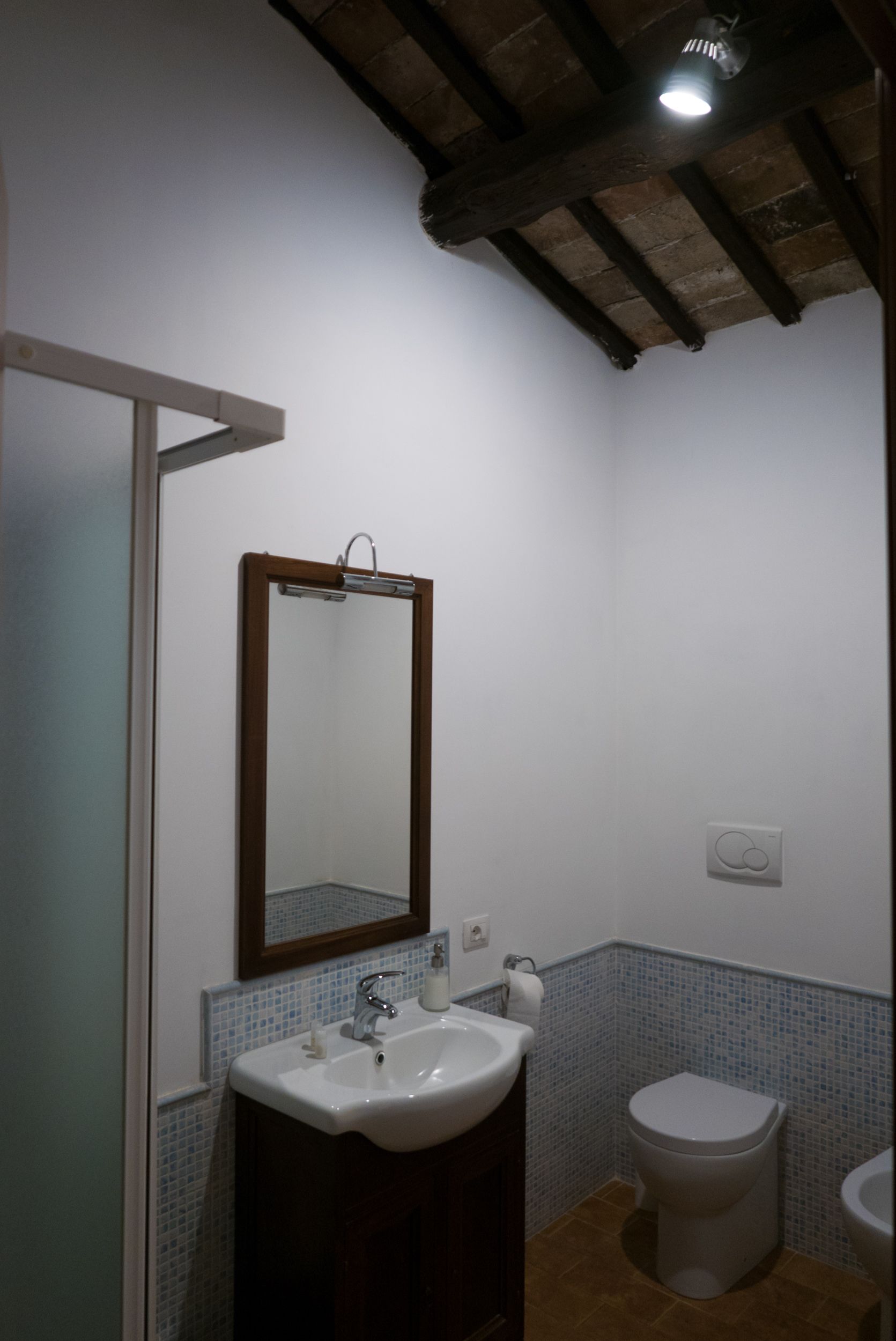Casa de banho com lavatório branco, espelho, sanita e zona de duche.
