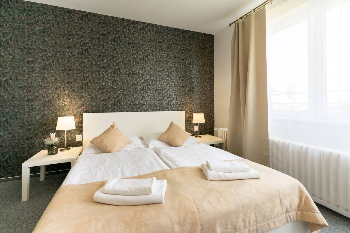 Quarto de hotel com uma cama grande, duas mesas de cabeceira, luminárias e vista para o exterior.