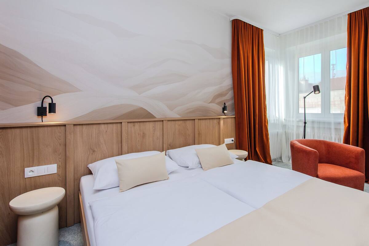 Quarto de hotel com uma cama, uma cadeira, uma mesa e um abajur.