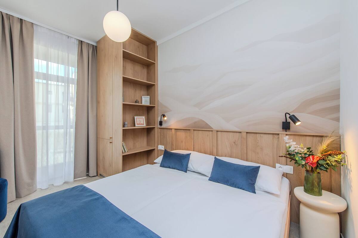 Quarto moderno com cama grande, estantes de madeira e luminária pendente.