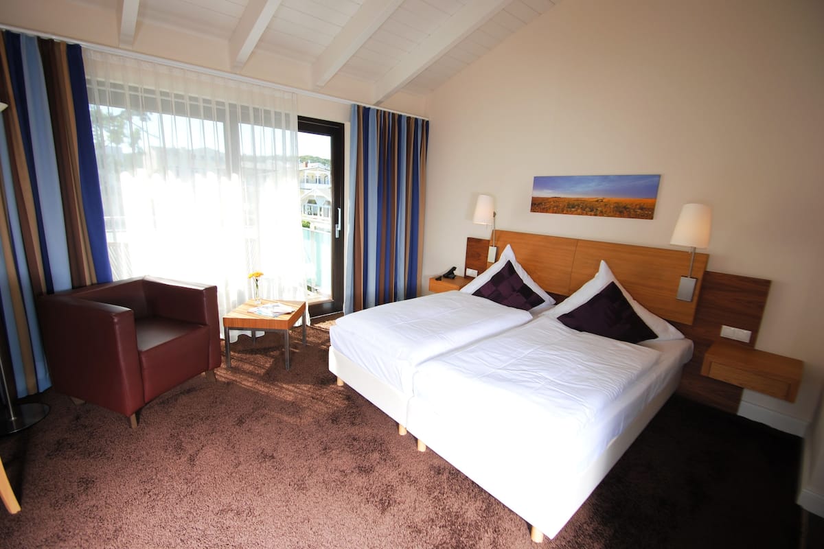 Quarto de hotel com uma cama grande, uma mesa, uma cadeira e vista para uma piscina pela janela.