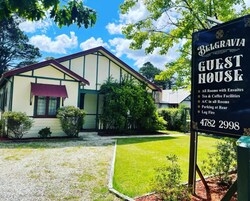 Uma residência de hóspedes com placa indicando comodidades como quartos privativos, serviço de chá e café, ar condicionado em todos os quartos, estacionamento na parte de trás e lareira.