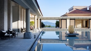 Área de piscina com espreguiçadeiras, um vaso grande e vista para o mar e as montanhas.