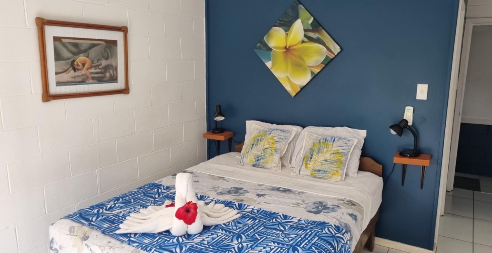Quarto de hotel com uma cama, um quadro pendurado na parede e uma mesa de cabeceira com abajur.