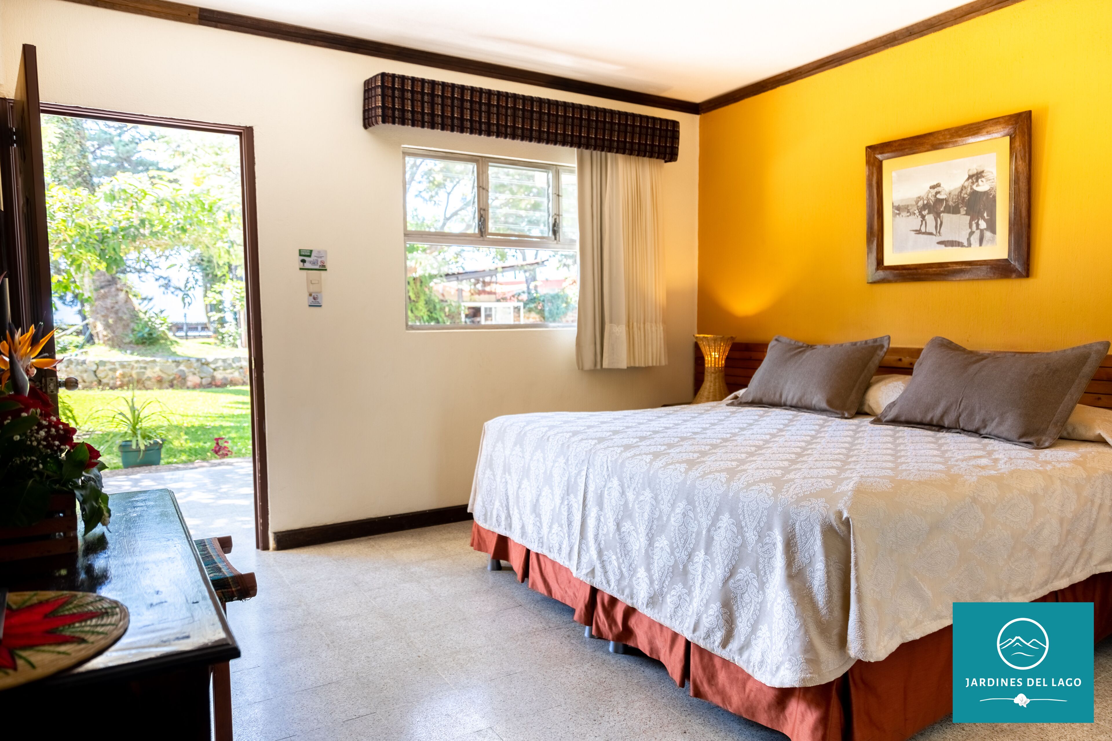 Um quarto com cama, janela, porta e vista para um jardim.