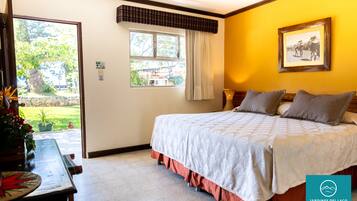 Um quarto com cama, janela, porta e vista para um jardim.