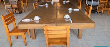 Uma ampla sala de jantar com mesas e cadeiras de madeira, uma cozinha ao fundo e uma placa com a inscrição "Jardines del Lago".