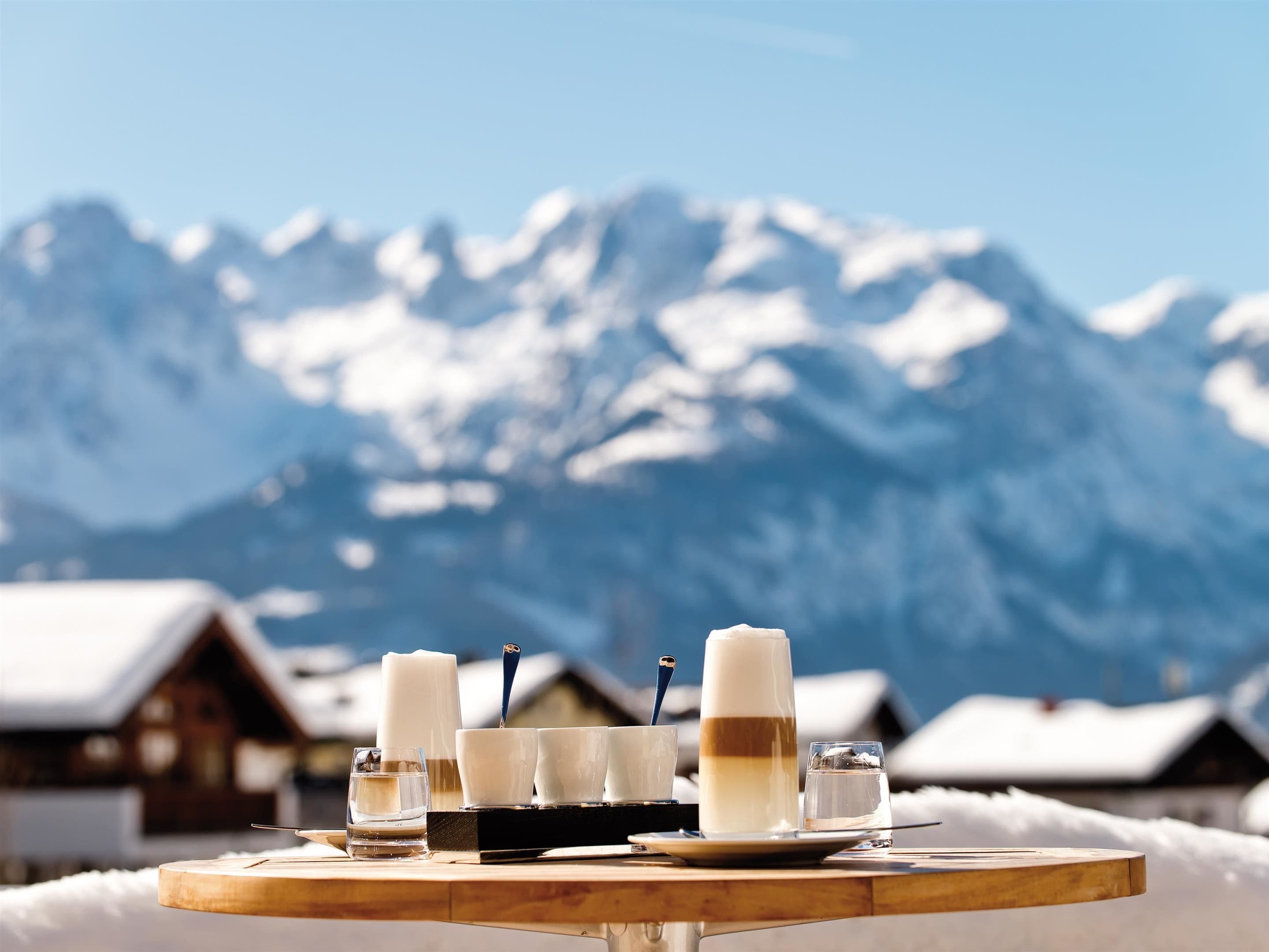 Uma mesa com uma vela, copos e um bule em um cenário montanhoso coberto de neve.