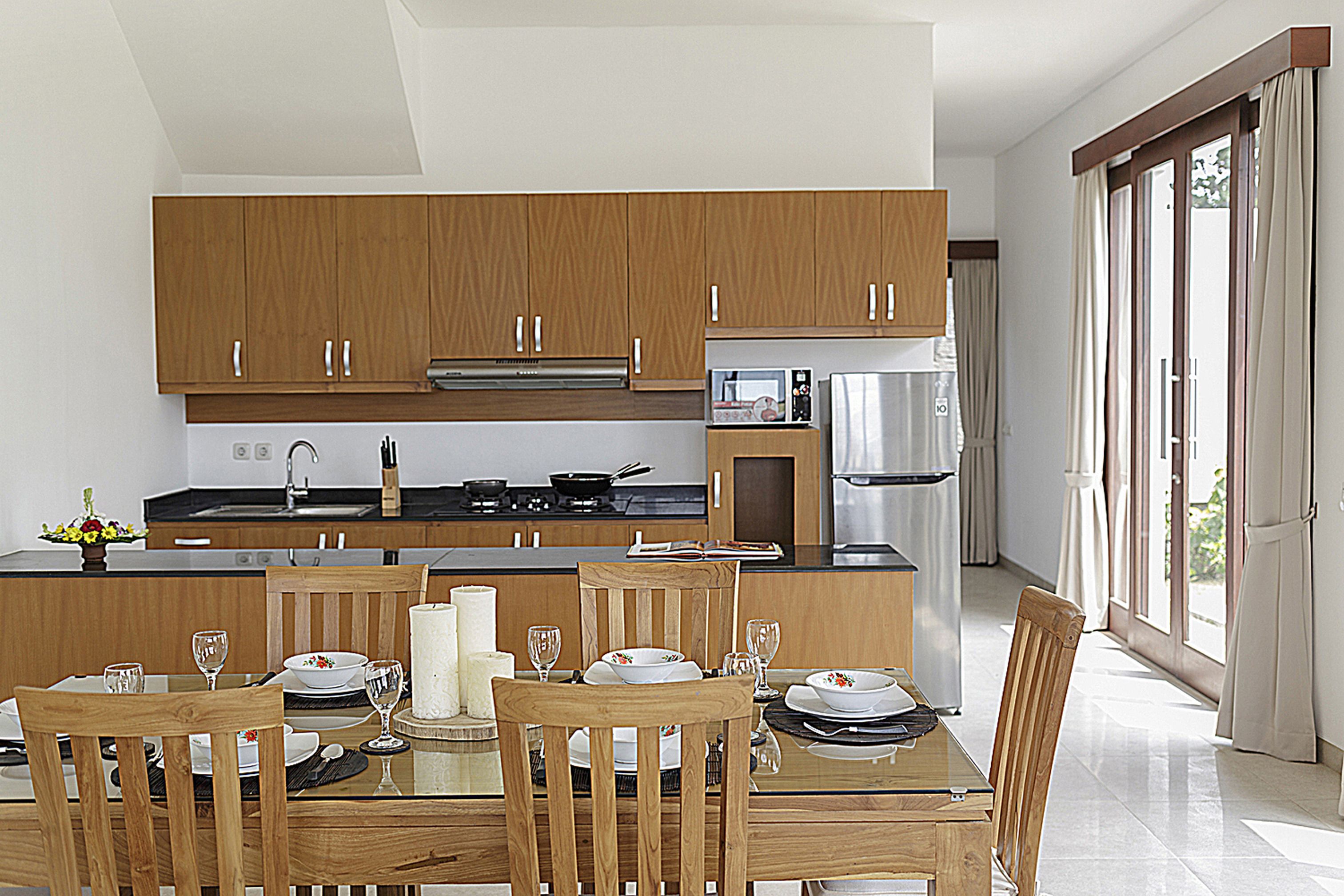 Cozinha moderna com armários de madeira, uma ilha central e uma área de jantar com mesa e cadeiras de vidro.