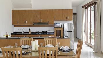 Cozinha moderna com armários de madeira, uma ilha central e uma área de jantar com mesa e cadeiras de vidro.