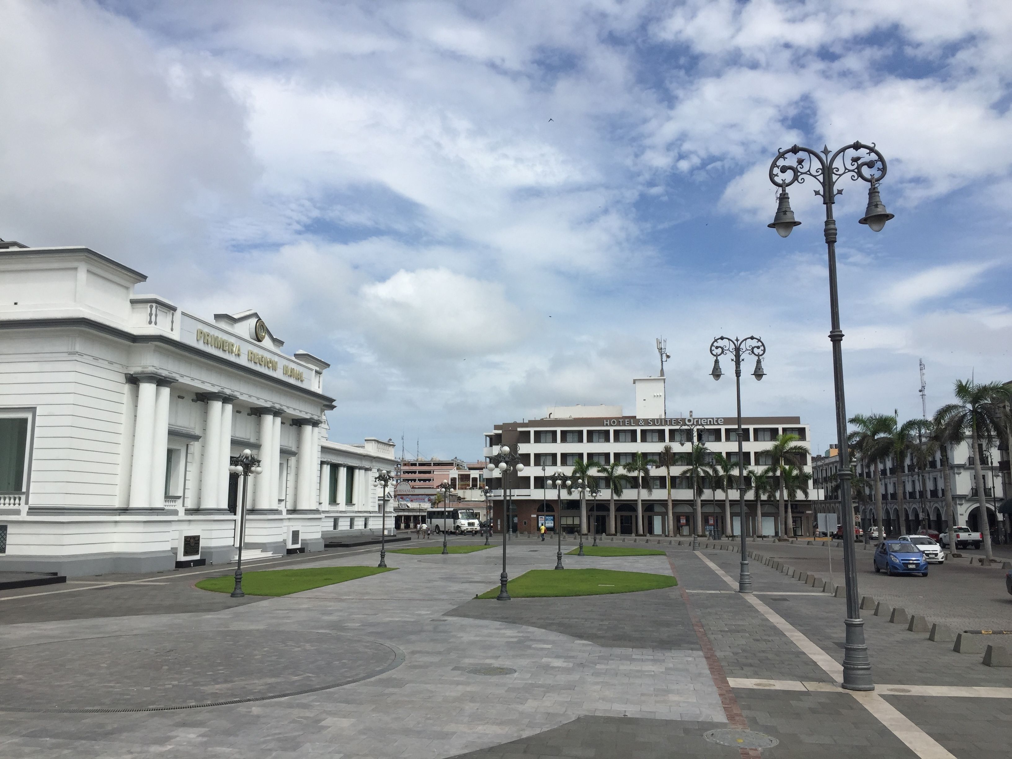 Um hotel com um pátio central, um edifício branco com colunas e uma construção de vários andares ao fundo.