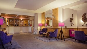 Um saguão de hotel com área de bar, assentos roxos e painéis de madeira.