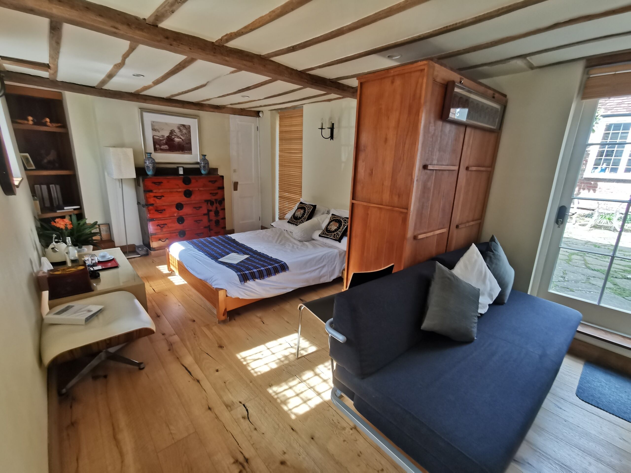 Quarto compacto com cama, sofá, escrivaninha e guarda-roupa.