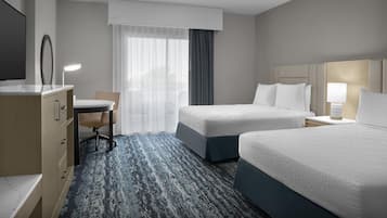 Quarto de hotel com duas camas, uma mesa, uma cadeira, uma televisão e uma janela com cortinas.