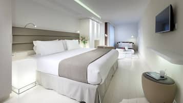 Quarto de hotel moderno com uma cama grande, mesas de cabeceira, televisão e uma pequena área de estar.