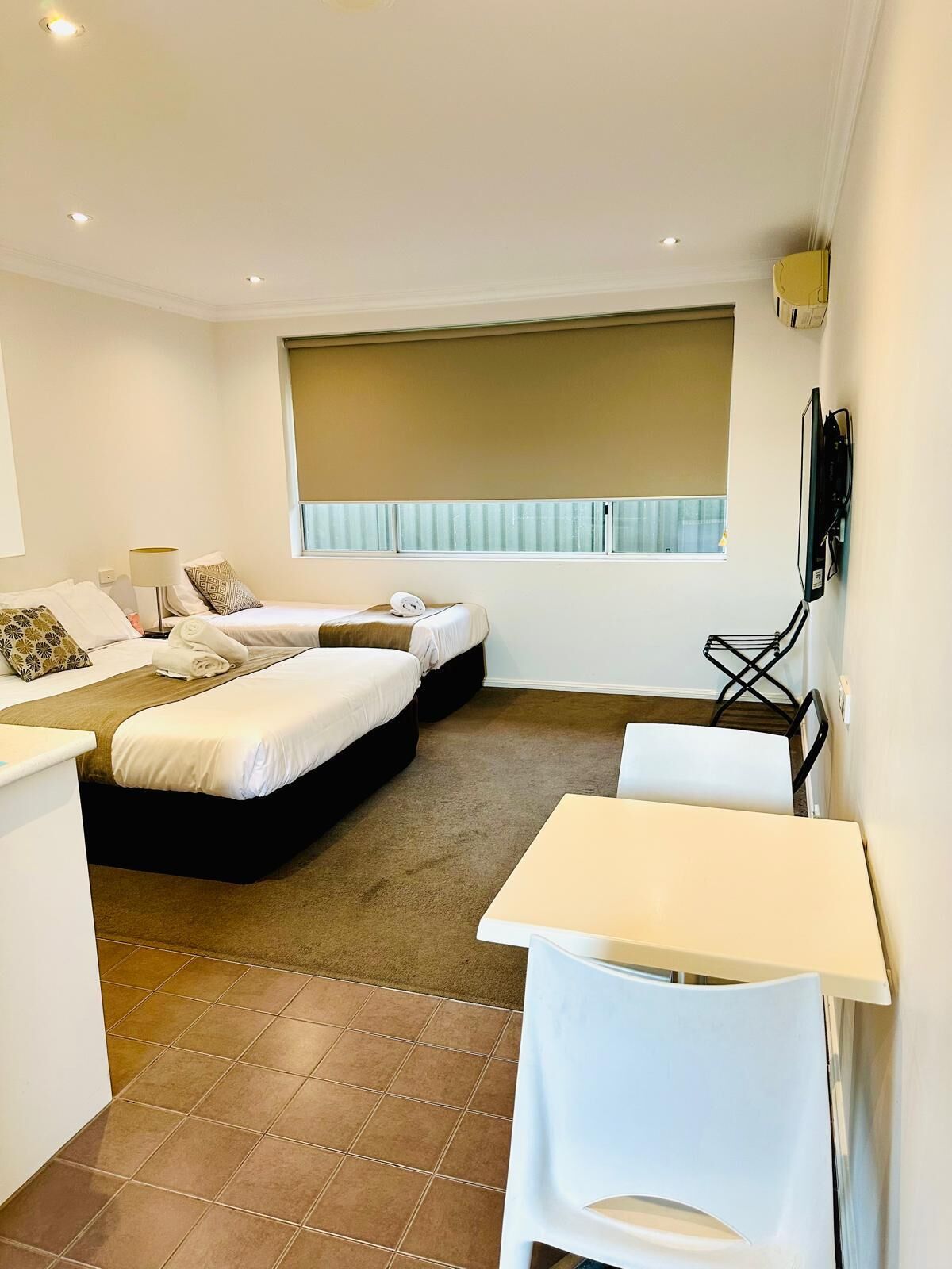 Quarto de hotel pequeno com duas camas, uma mesinha e uma televisão fixada na parede.