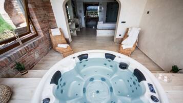 Uma área de spa com hidromassagem, cadeiras de vime e vista para o quarto ao fundo.